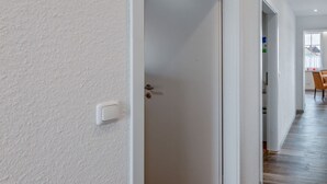 Corredor com parede branca texturizada, uma porta e uma janela com vista para uma varanda.