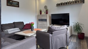 Uma sala de estar moderna com um sofá, poltronas, uma mesa de centro, uma televisão e uma placa com a inscrição 'LOUNGE'.