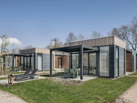 Uma área de estar moderna ao ar livre, com duas cadeiras de descanso e uma mesa, cercada por paredes de vidro e painéis de madeira.