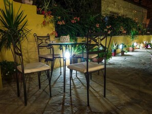 Uma área de pátio com mesa e quatro cadeiras, rodeada por plantas e flores em vasos.