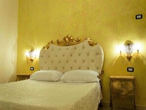 Quarto com cabeceira estofada, cama com roupa de cama branca e duas arandelas na parede.