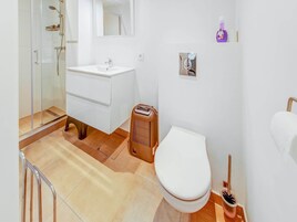 Casa de banho com cabine de duche em vidro, lavatório branco, sanita e chuveiro manual.