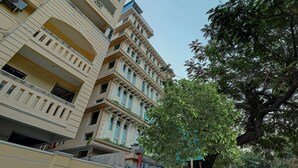 Um edifício de vários andares com varandas e uma grande árvore em primeiro plano.