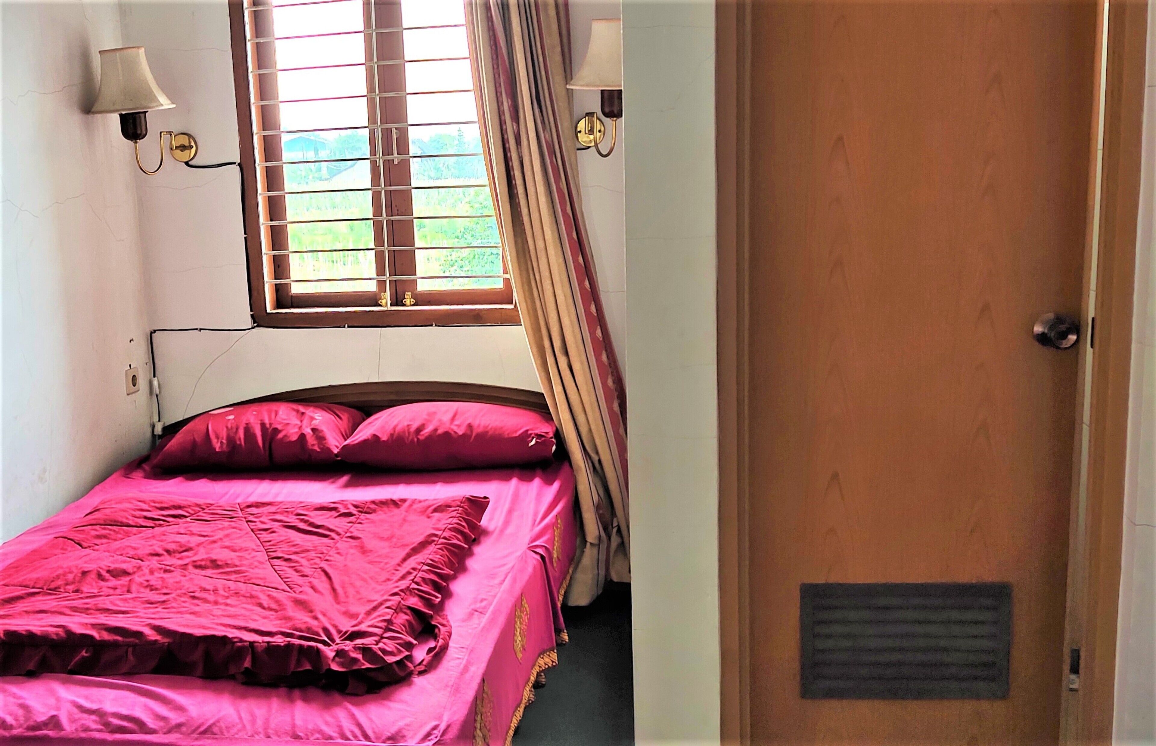 Um quarto com uma cama, uma janela com cortinas e uma porta.