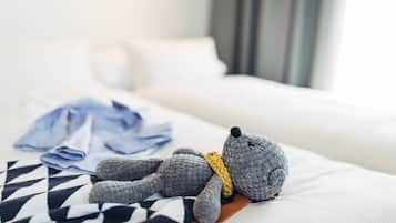Uma cama com um brinquedo de pelúcia cinza, uma camisa azul e um cobertor estampado.