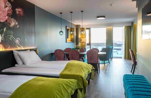 Quarto de hotel com duas camas, uma escrivaninha com cadeiras, uma janela ampla com vista e uma varanda.