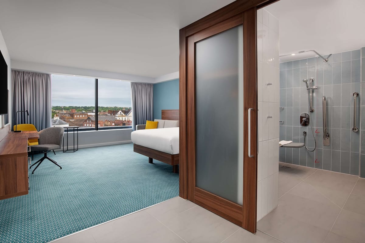 Quarto de hotel com cama, escrivaninha, cadeira e vista para a cidade.
