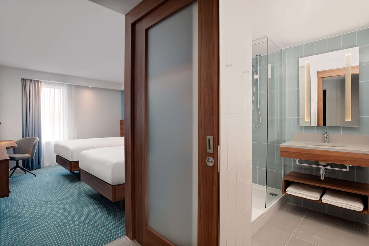 Quarto de hotel com cama, escrivaninha e chuveiro.