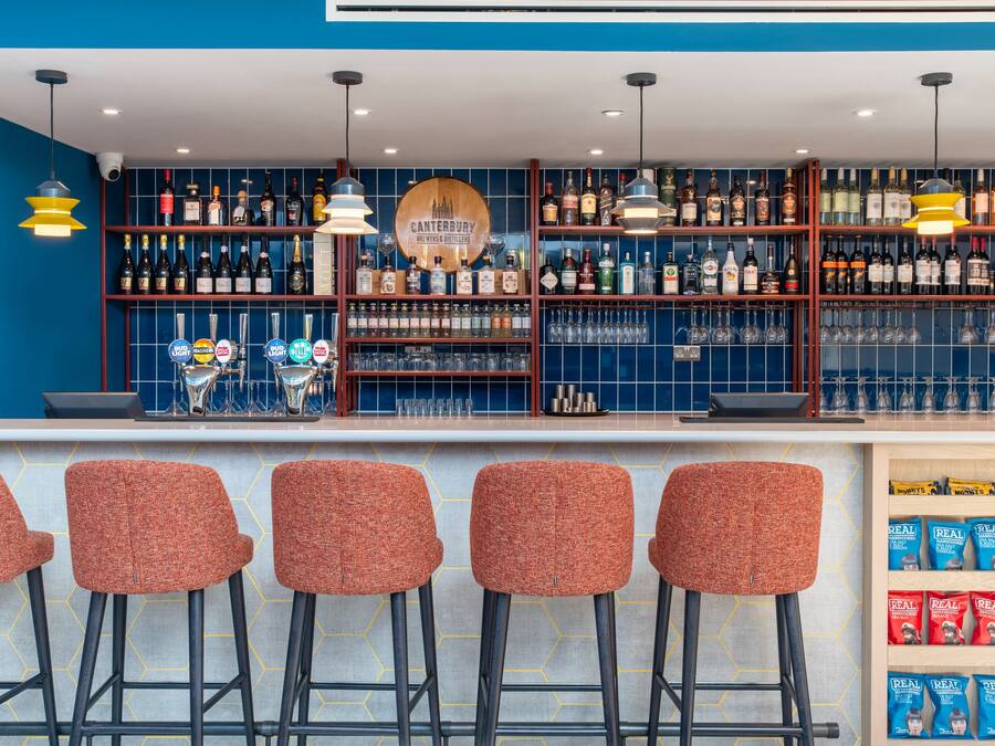 Um bar com várias prateleiras de garrafas de bebidas, um balcão e quatro banquetas vermelhas.
