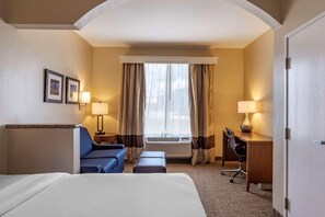 Quarto de hotel com cama, escrivaninha, cadeira, sofá e janela com cortinas.