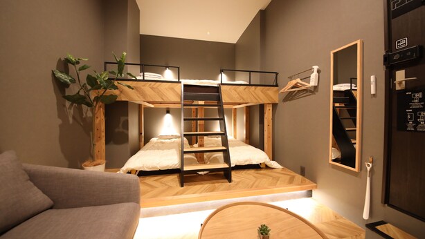 Quarto com beliches, uma mesinha com planta, um sofá e um espelho na parede.