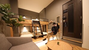 Quarto moderno com beliches, sofá, mesa de madeira redonda e planta em vaso.