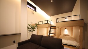 Quarto compacto com uma cama beliche, um sofá e uma pequena planta.