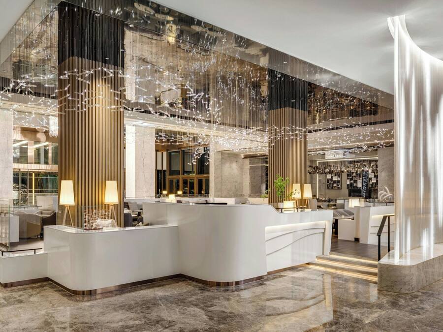 Um hall de hotel moderno com um balcão de recepção curvo, piso de mármore e luminárias contemporâneas.