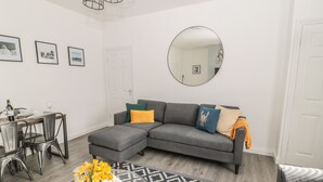 Uma sala de estar moderna com um sofá seccional cinza, um espelho redondo e uma área de jantar com cadeiras de metal e uma mesa de vidro.