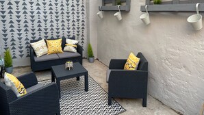 Uma área de pátio com parede estampada, móveis de exterior e plantas em vasos.