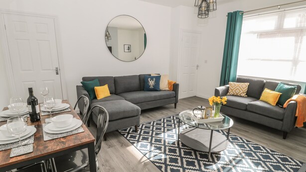 Uma sala de estar moderna com área de jantar, sofás cinzas com almofadas estampadas, uma mesa de centro redonda e um tapete estampado.