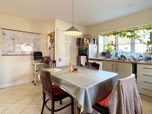 Uma área de refeições com mesa, cadeiras, uma luminária pendente e vista para a cozinha.