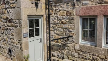 Um edifício de pedra com uma porta e janelas brancas, um poste de luz preto e uma placa com a inscrição 'Green Farm Cottage'.