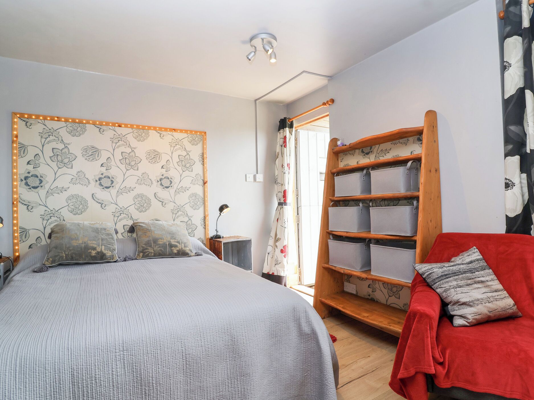 Um quarto com uma cama, uma mesa de cabeceira, uma estante de livros e uma cadeira vermelha.