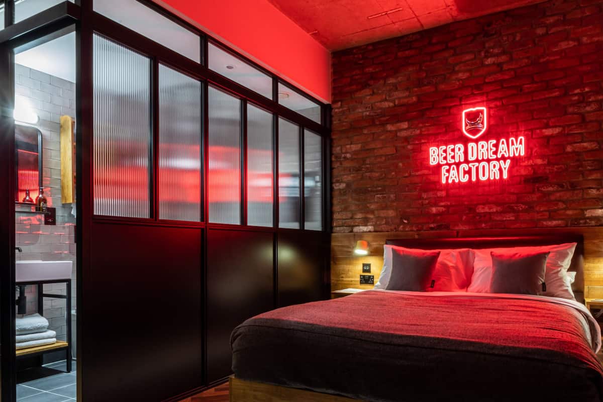 Quarto moderno com uma cama grande, um letreiro de neon que diz 'Beer Dream Factory' e uma parede de tijolos.