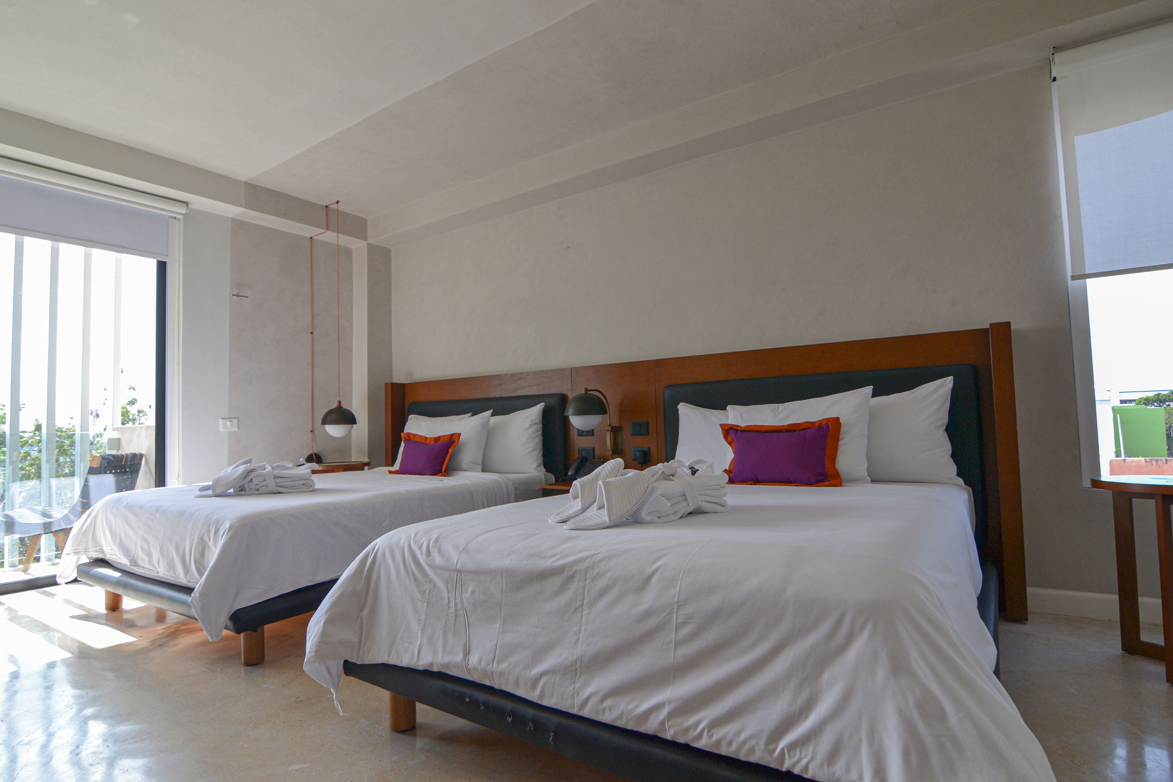 Quarto de hotel com duas camas, uma janela grande e vista para o exterior.