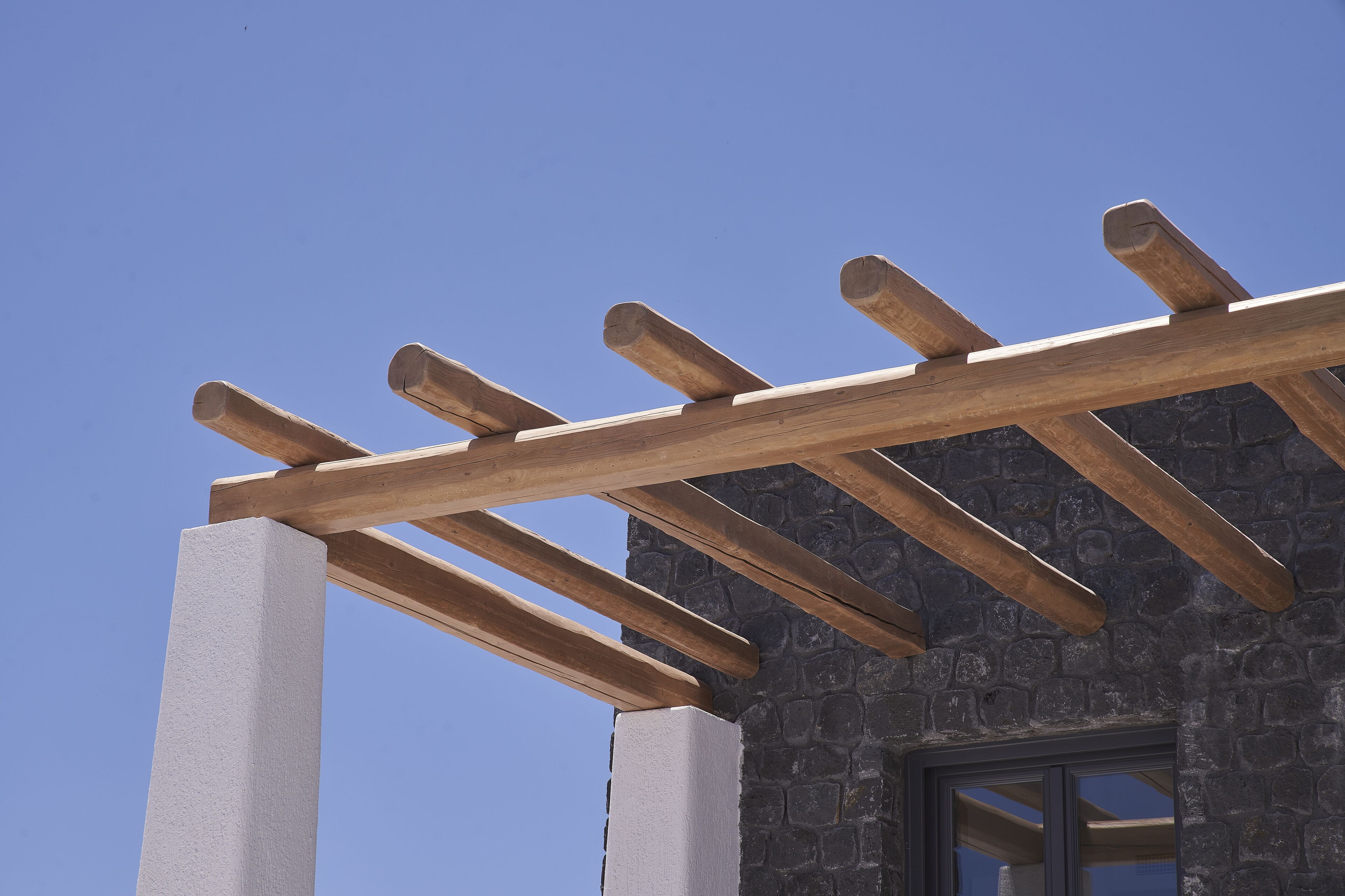 Uma estrutura de pérgola de madeira com parede de pedra e uma janela.
