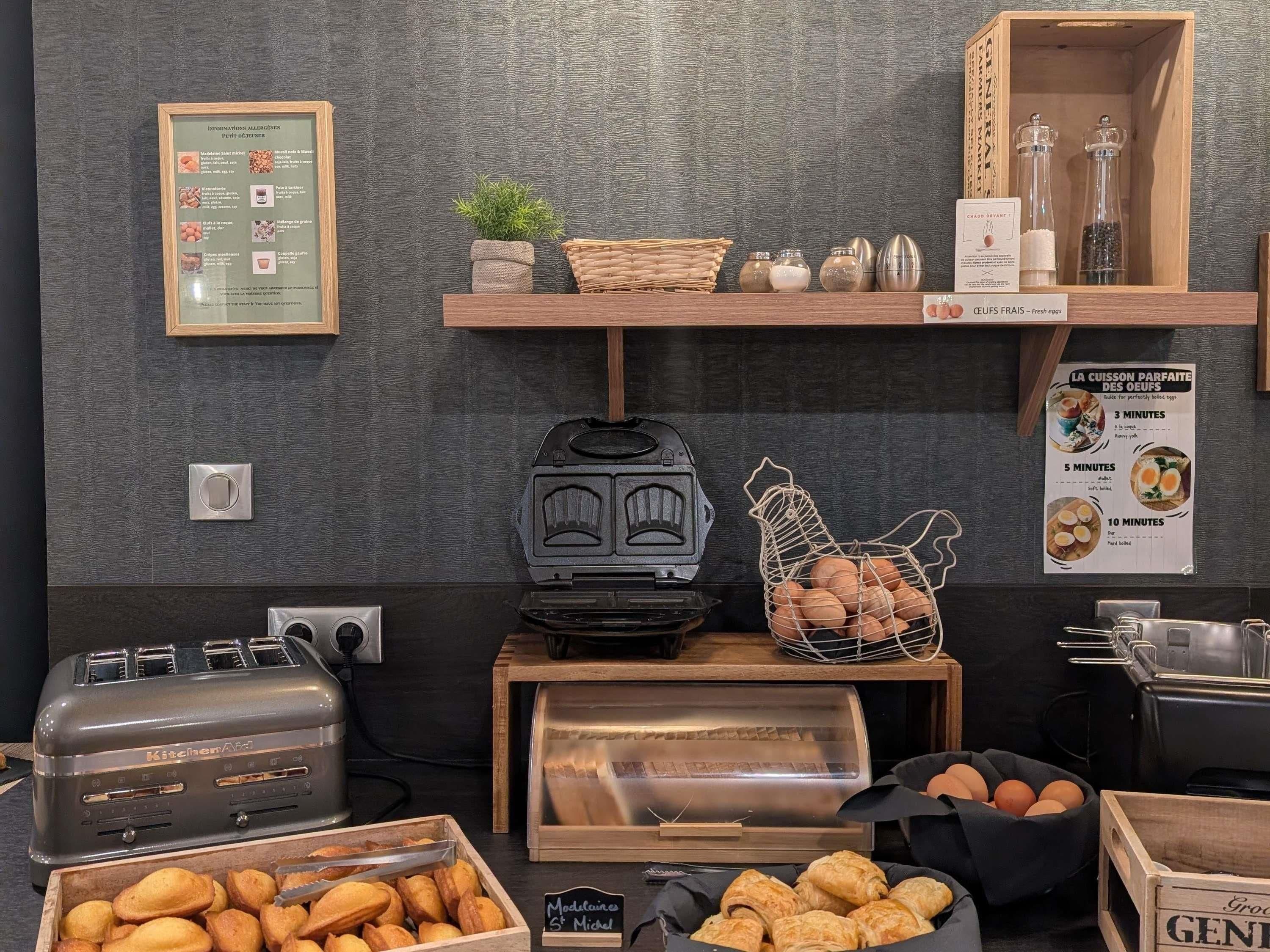 Uma estação de café da manhã com cardápio, torradeira, pães, croissants e uma vitrine com ovos.