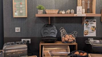 Uma estação de café da manhã com cardápio, torradeira, pães, croissants e uma vitrine com ovos.