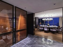 Uma área de jantar moderna com uma mesa redonda posta para seis pessoas, rodeada por cadeiras, e um grande candelabro acima.