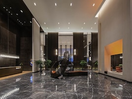 Um lobby moderno com piso de mármore, um balcão de recepção e uma grande escultura abstrata.