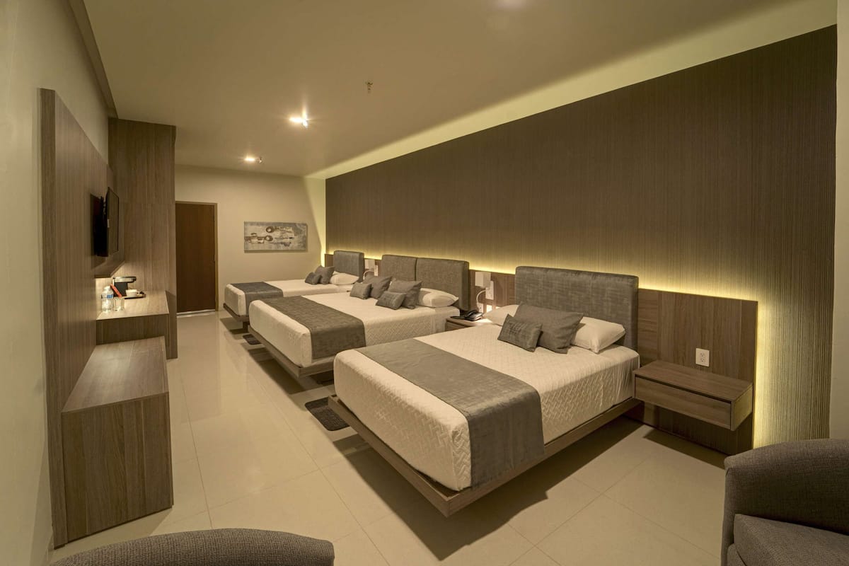 Quarto de hotel moderno com duas camas, televisão, escrivaninha e uma grande obra de arte na parede.