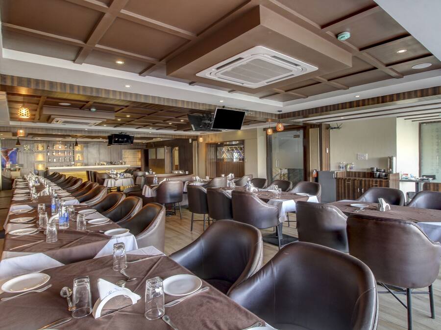 Um restaurante com mesas grandes e partilhadas, e também cabines individuais, com talheres e um ecrã de televisão.