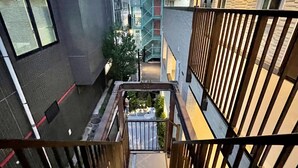 Uma escadaria leva a um edifício com guarda-corrimão de metal, com vista para a rua e para um edifício com fachada de tijolos.