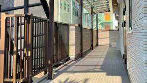 Uma galeria coberta com painéis de vidro e guarda-corpos de metal, que conduz a um edifício com fachada de tijolos.