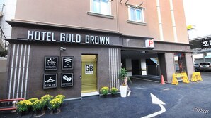 Exterior do Hotel Gold Brown com uma placa indicando uma área de estacionamento.