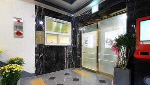 Uma área de recepção com parede de mármore, balcão de atendimento, planta e um quiosque de informações vermelho.