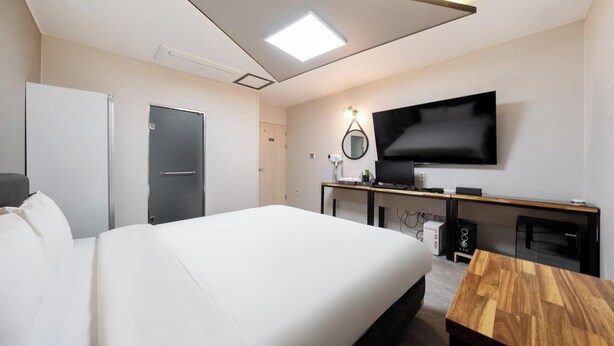 Quarto de hotel com cama, escrivaninha, televisão de tela plana, espelho e armário.