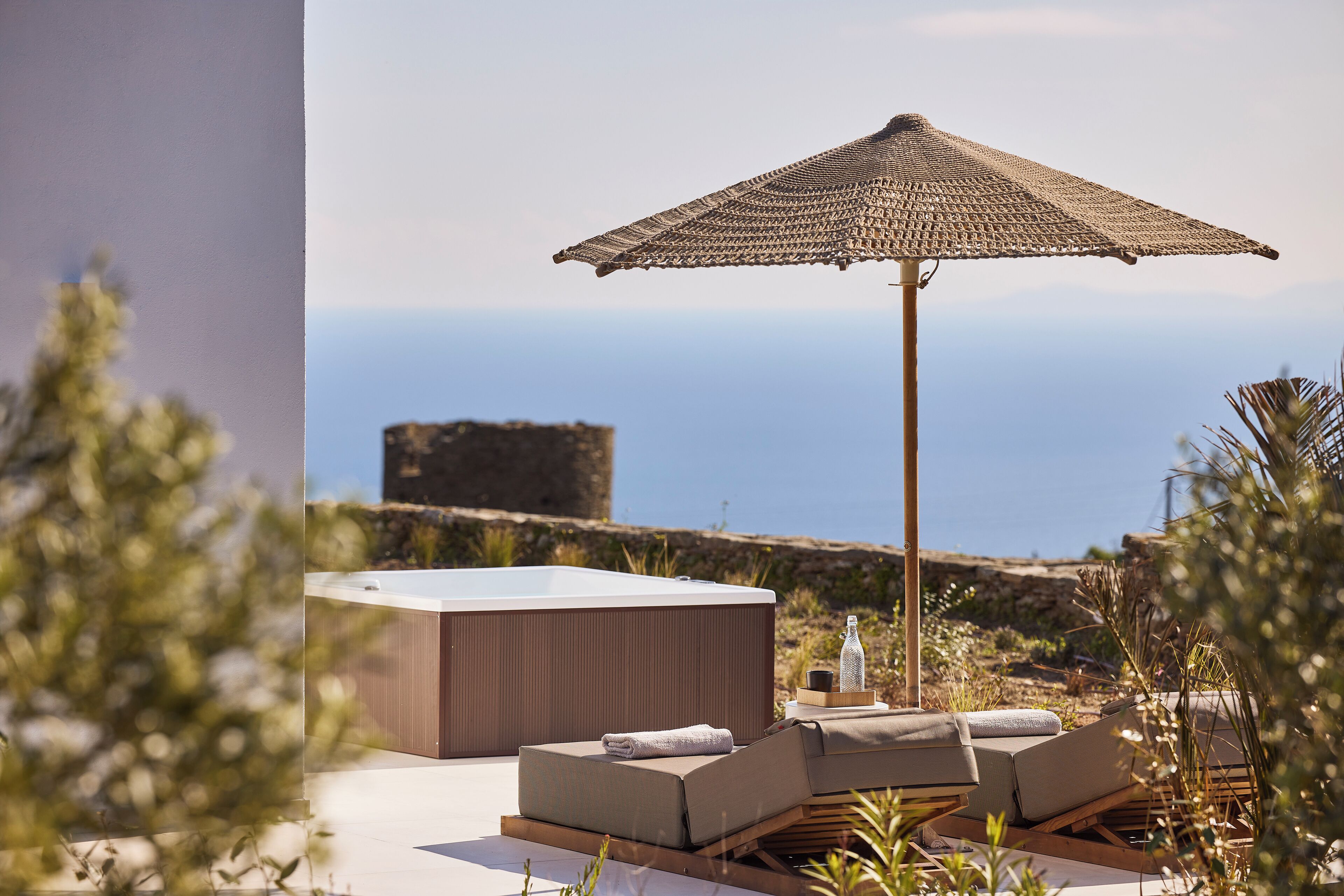 Um lounge no terraço com um grande guarda-sol, cadeiras de descanso e vista para o mar.