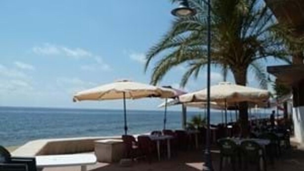 Um terraço à beira-mar com mobiliário de exterior e guarda-sóis, com vista para o oceano.