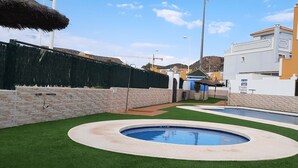 Uma piscina com design circular, rodeada por relvado sintético, adjacente a um muro de pedra.