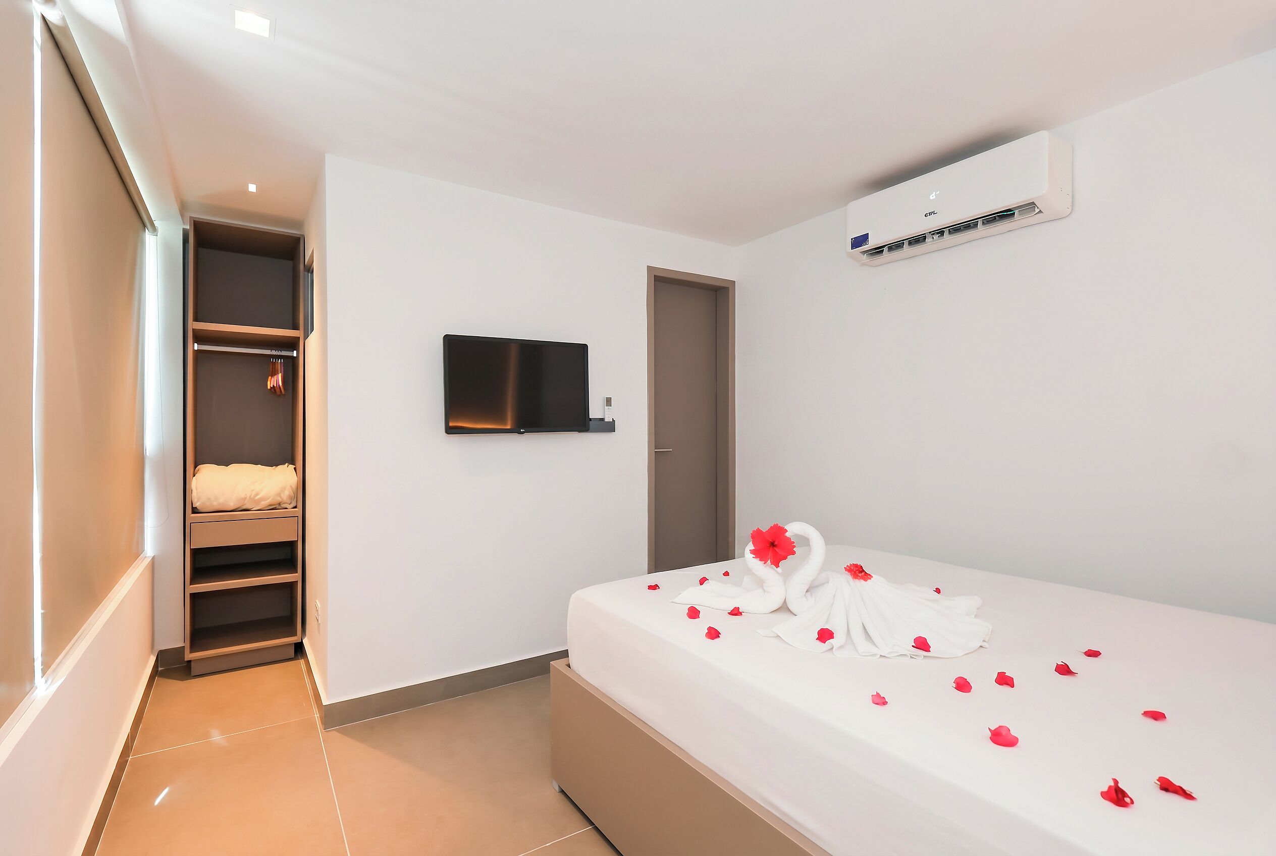 Quarto de hotel com cama, televisão, guarda-roupa e ar condicionado.