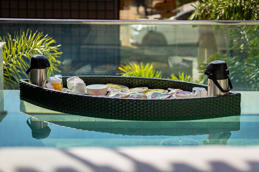Uma mesa de vidro com um tabuleiro trançado contendo diversos alimentos e duas garrafas térmicas.
