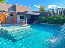 Piscina com área de bar, boia salva-vidas e um edifício moderno com porta de madeira.