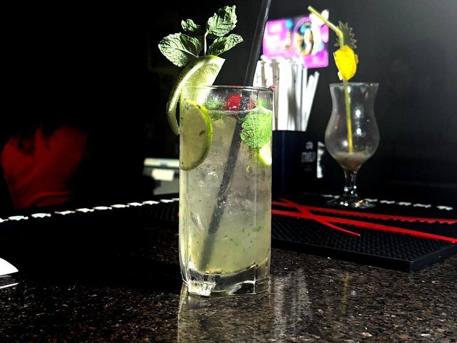 Um cocktail com rodela de limão e folhas de hortelã sobre um balcão de bar.