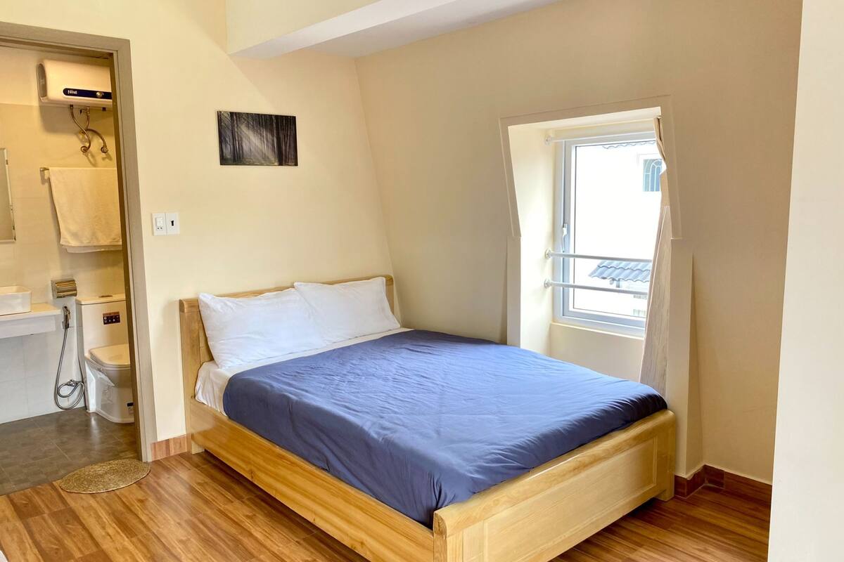 Quarto com cama de madeira, janela com vista e banheiro com vaso sanitário e pia.