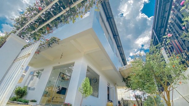 Um edifício moderno com entrada coberta, grandes janelas e um jardim com diversas plantas e flores.