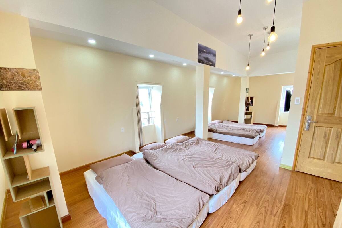 Quarto com duas camas, soalho de madeira, porta de madeira e uma janela.