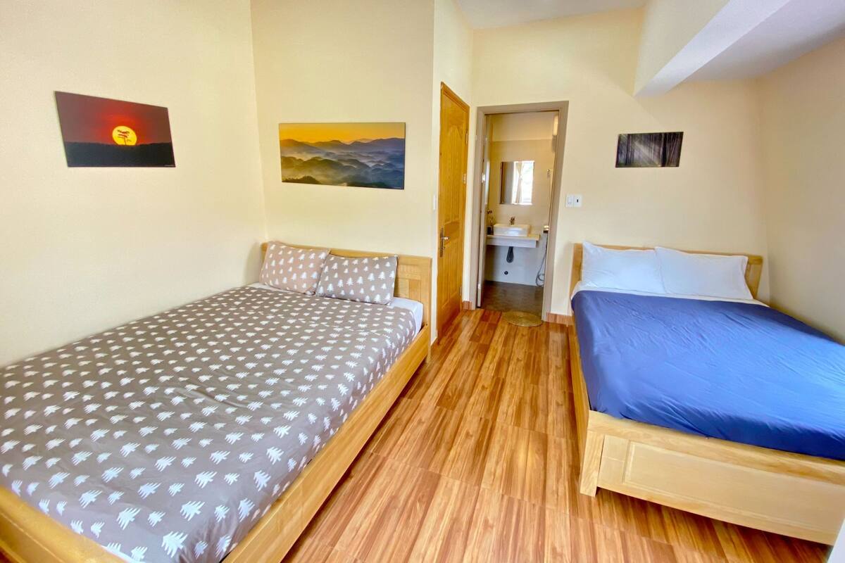 Quarto com duas camas, piso de madeira, banheiro com pia e porta que dá para outro cômodo.