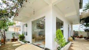 Uma casa moderna com porta de entrada de vidro, um pequeno jardim com plantas em vasos e uma área com pedriscos.